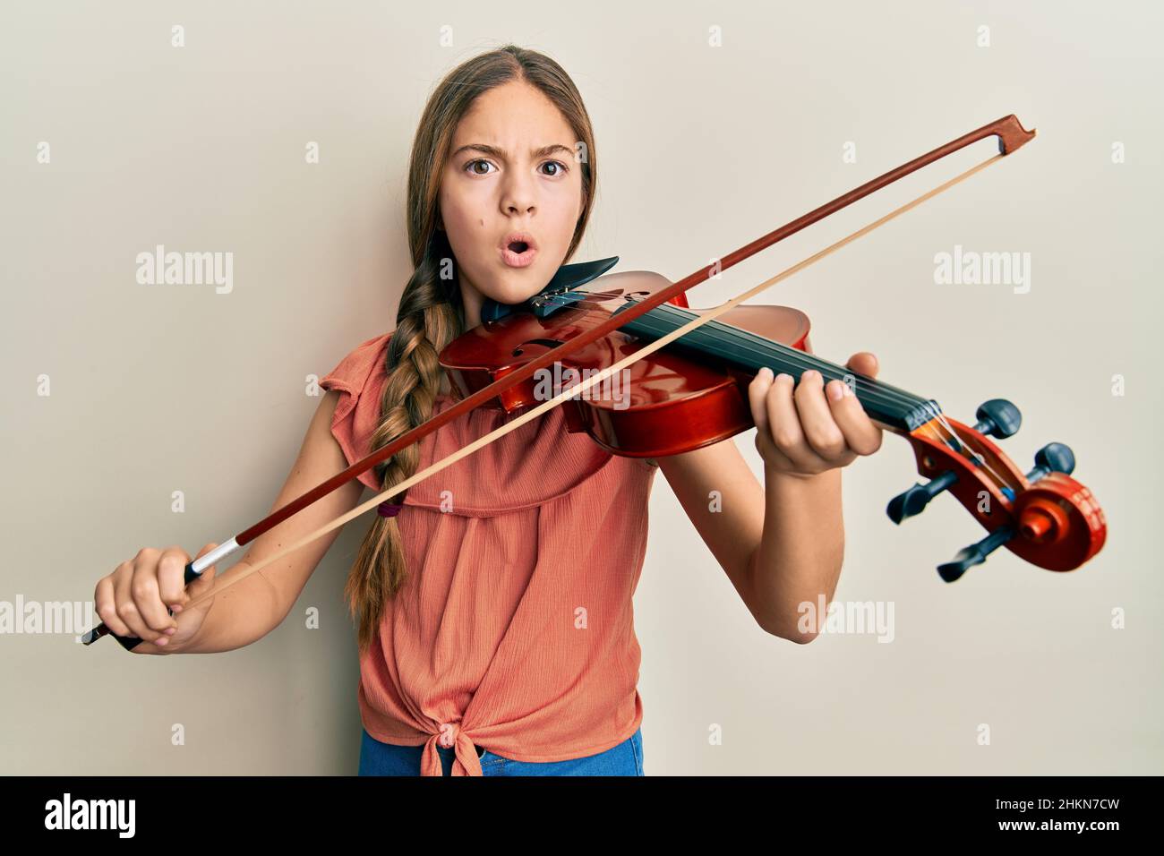 Beautiful brunette little girl playing violin in shock face, looking ...
