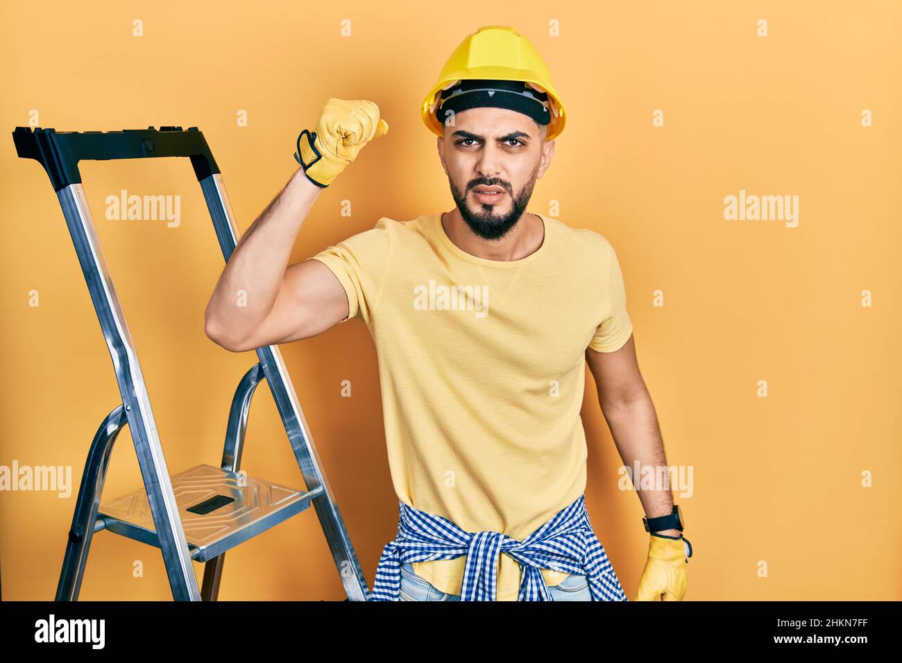 Handsome man with beard by construction stairs wearing hardhat angry ...