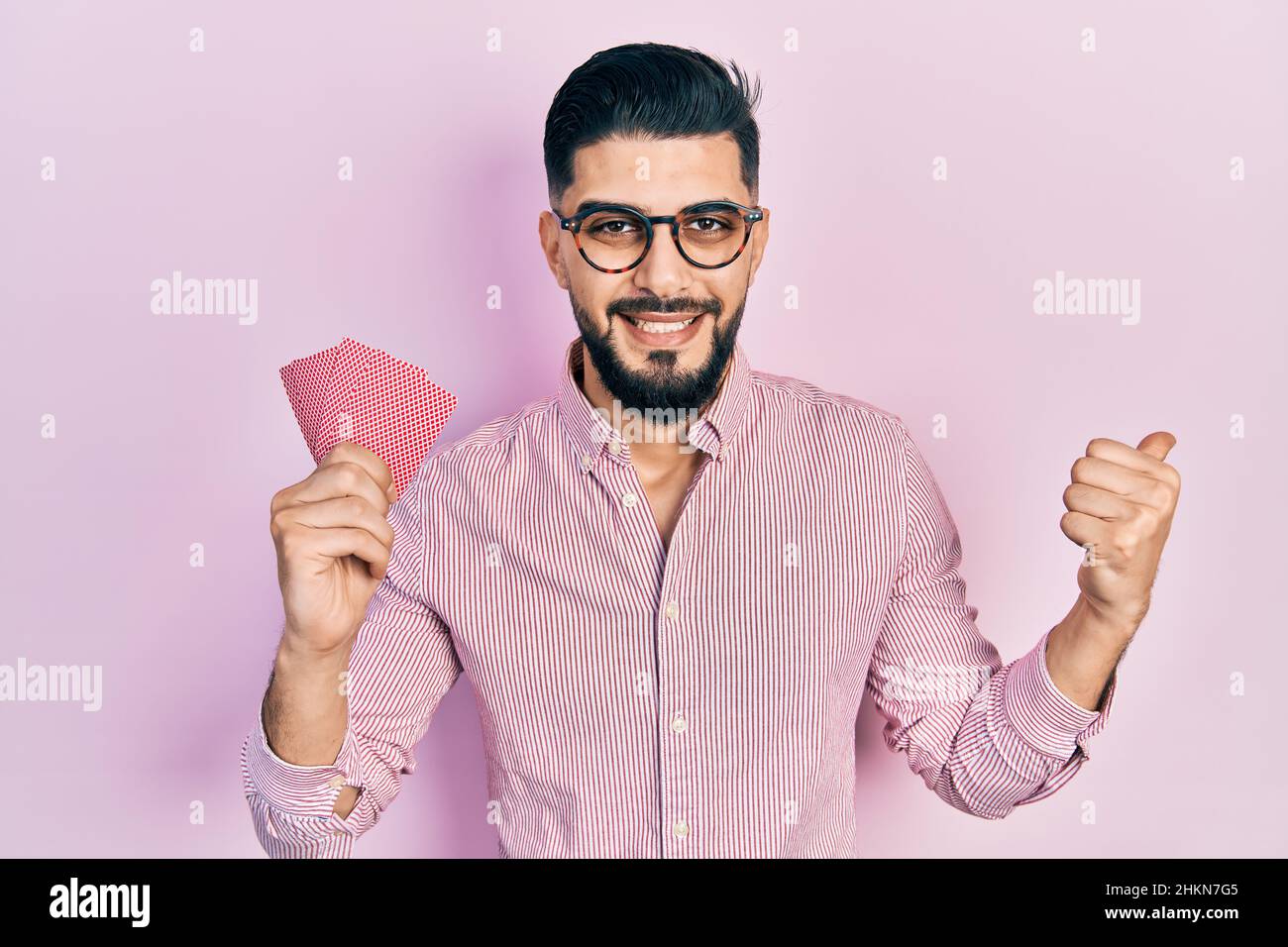 Handsome man with beard holding poker cards pointing thumb up to the ...