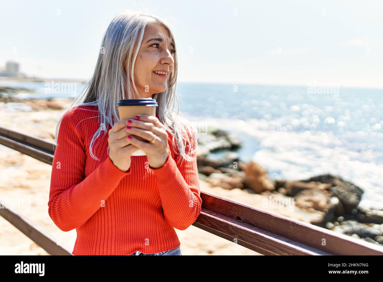 Middle age grey-haired woman smiling happy drinking coffee at the beach ...