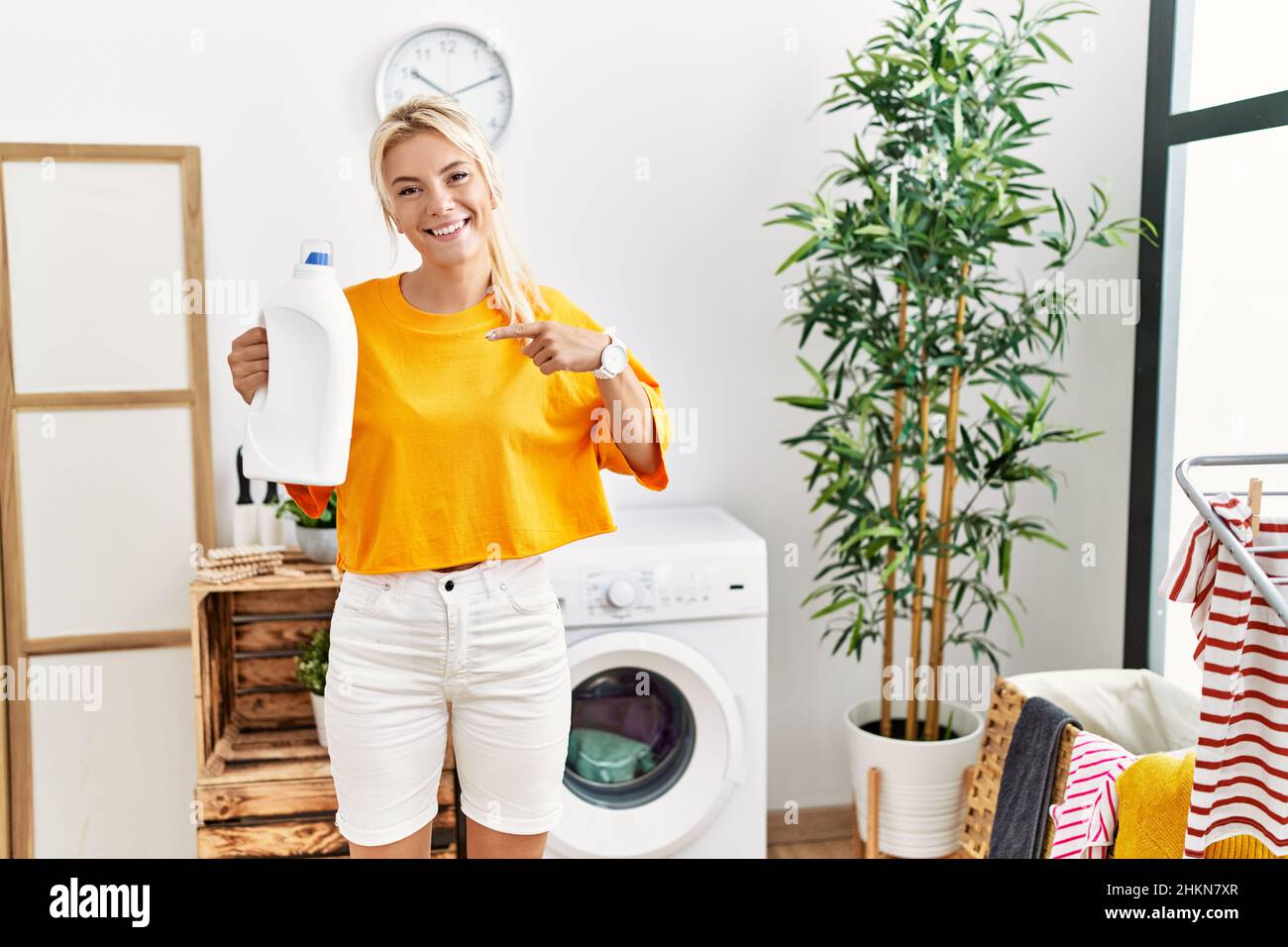 Young caucasian woman doing laundry holding detergent bottle smiling happy pointing with hand ...