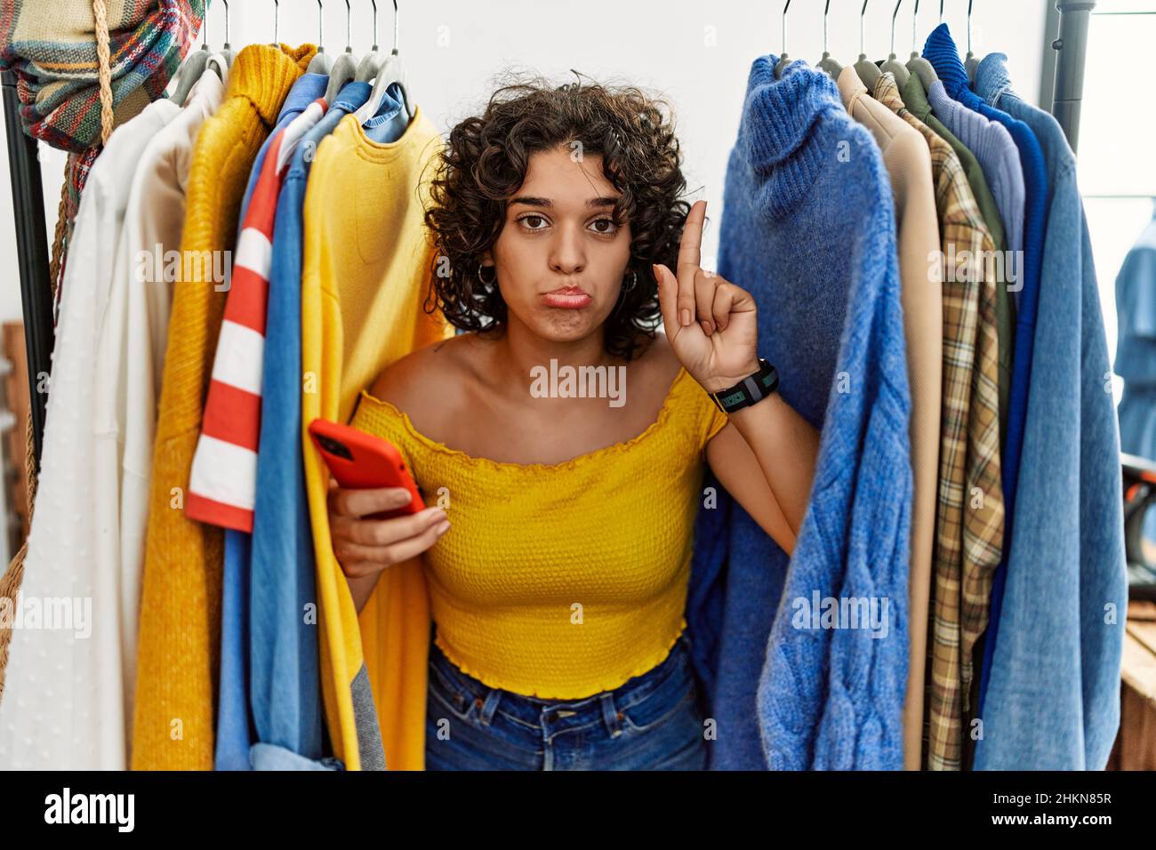 Young hispanic woman searching clothes on clothing rack using ...