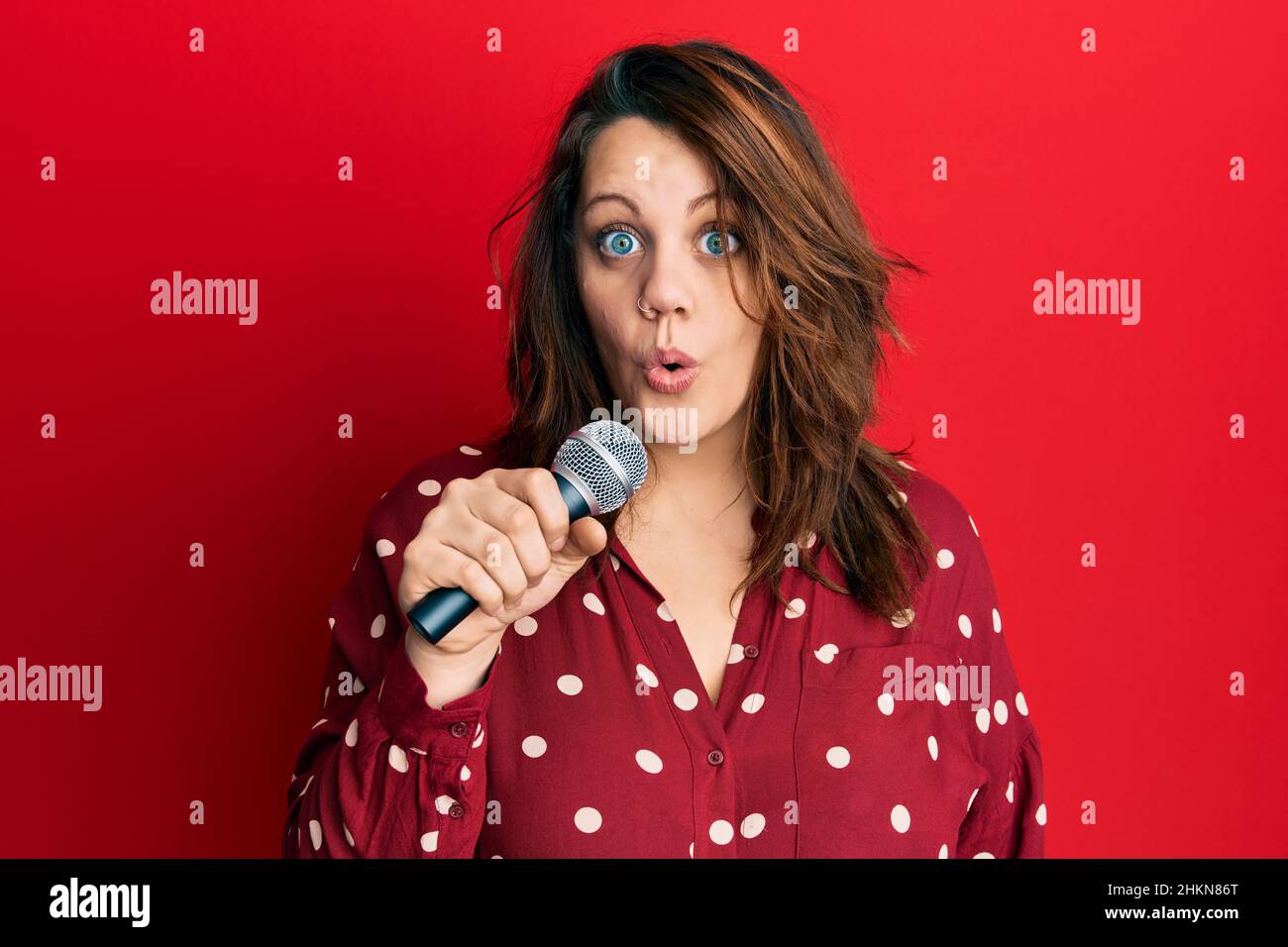 Young caucasian woman singing song using microphone scared and amazed ...
