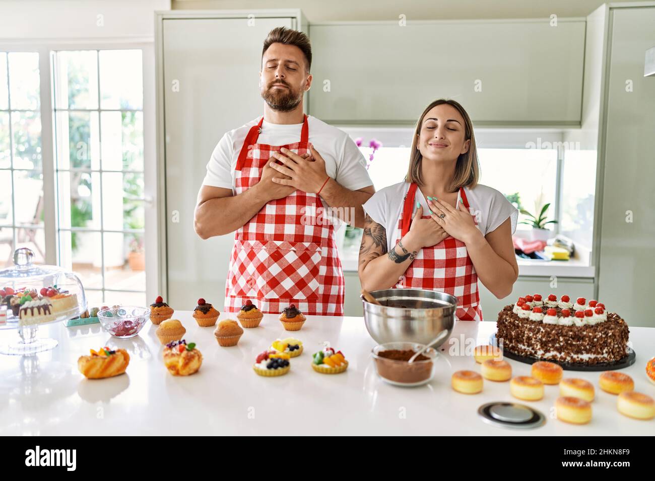 Young couple cooking pastries at the kitchen smiling with hands on ...