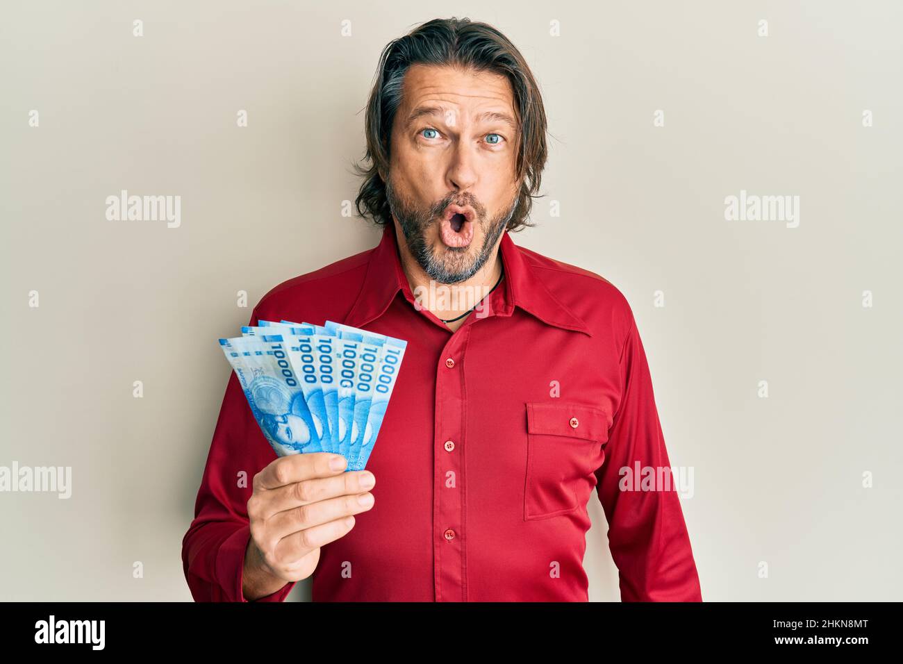 Middle age handsome man holding 10000 chilean pesos scared and amazed ...