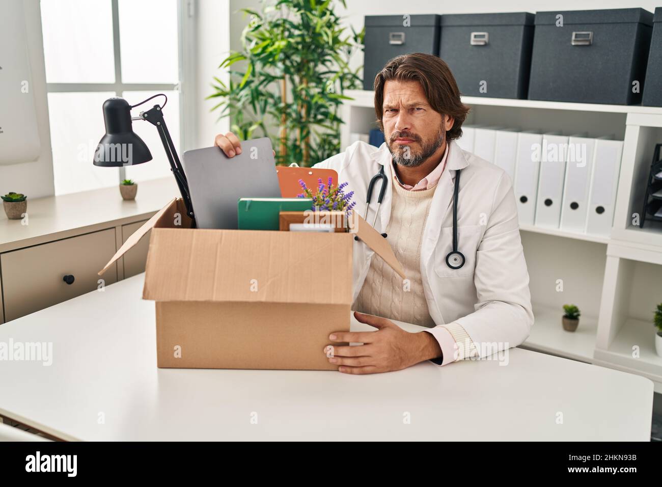 Handsome middle age doctor man holding box with items skeptic and ...