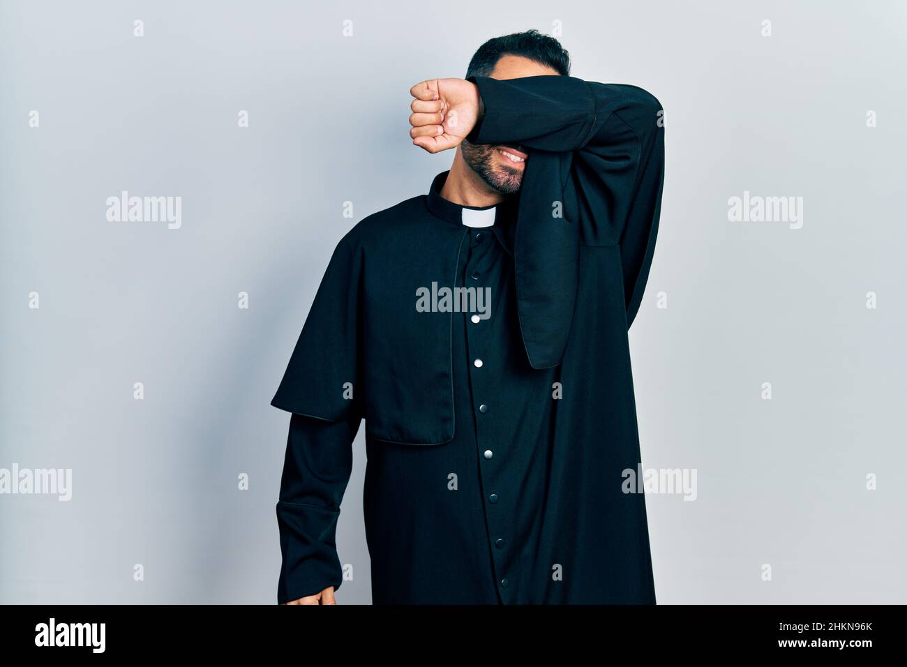 Handsome hispanic man with beard wearing catholic priest robe covering ...