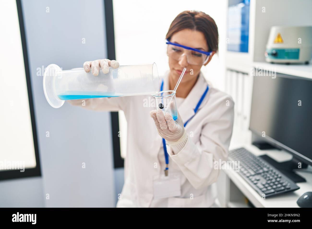 Young hispanic woman wearing scientist uniform measuring liquid at ...