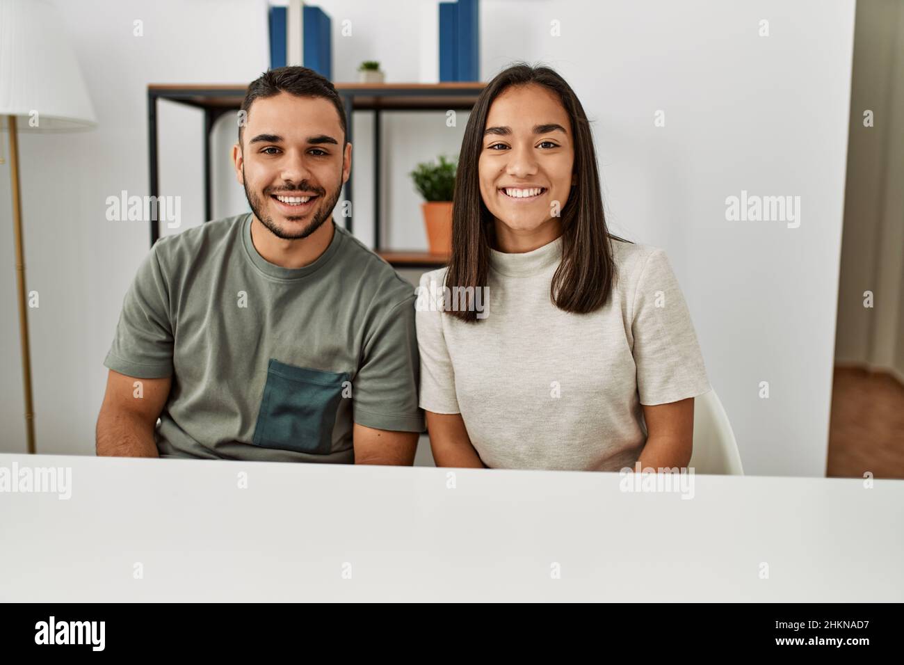 Young latin couple wearing casual clothes sitting on the table looking ...