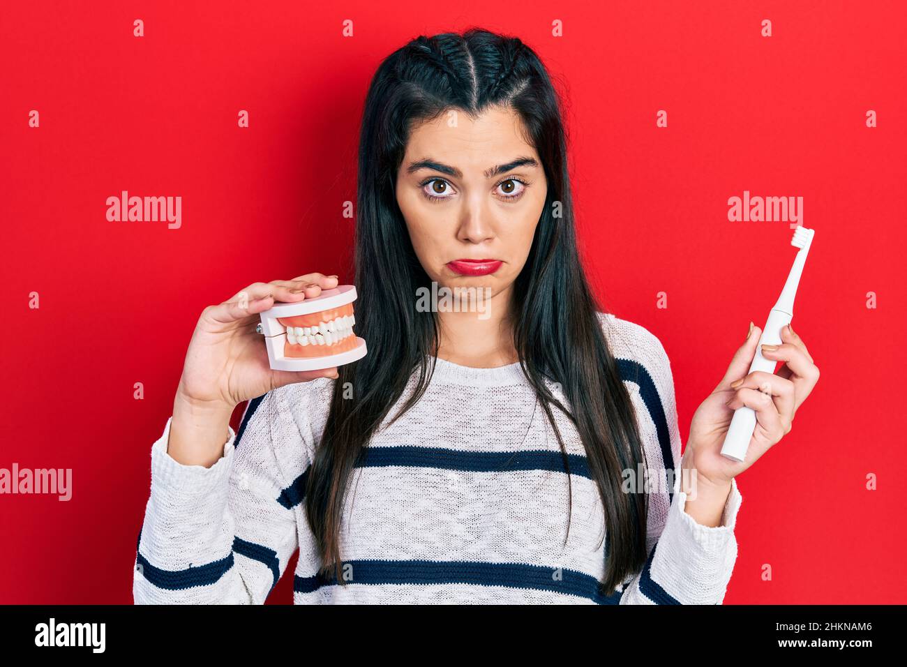 Young hispanic girl holding electric toothbrush and denture depressed ...