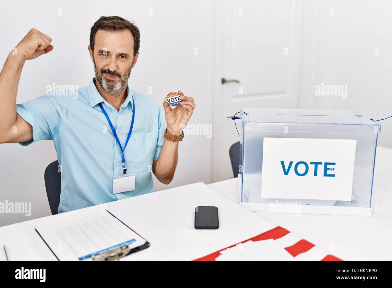 Middle age man with beard sitting by ballot holding i vote badge strong ...