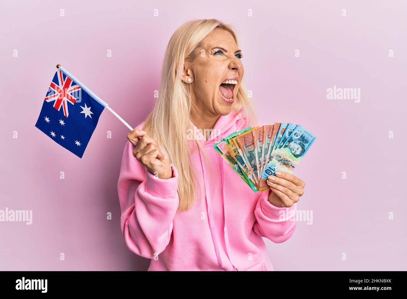 Young blonde woman holding australian flag and dollars angry and mad ...