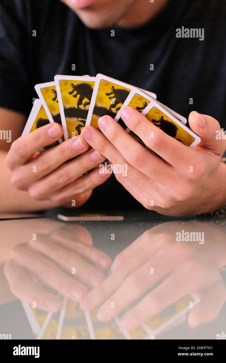 Young man playing One Night Ultimate Werewolf with hand of cards fanned ...