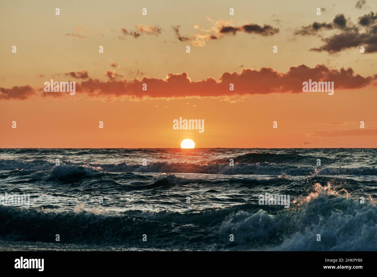 Half sun below horizon over blue sea waves, beautiful sunset over sea ...