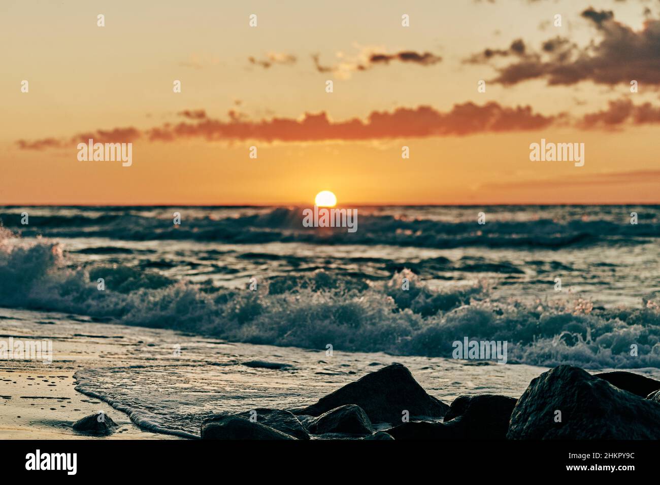 Yellow sun almost down horizon over deep blue sea at atmospheric sunset ...