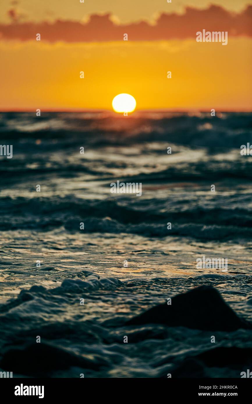 Yellow sun almost down horizon over deep blue sea at atmospheric sunset ...