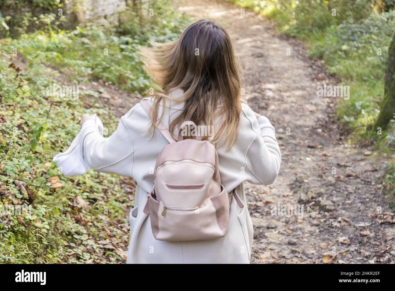 Back view of a young female with a pink backpack running in a forest ...