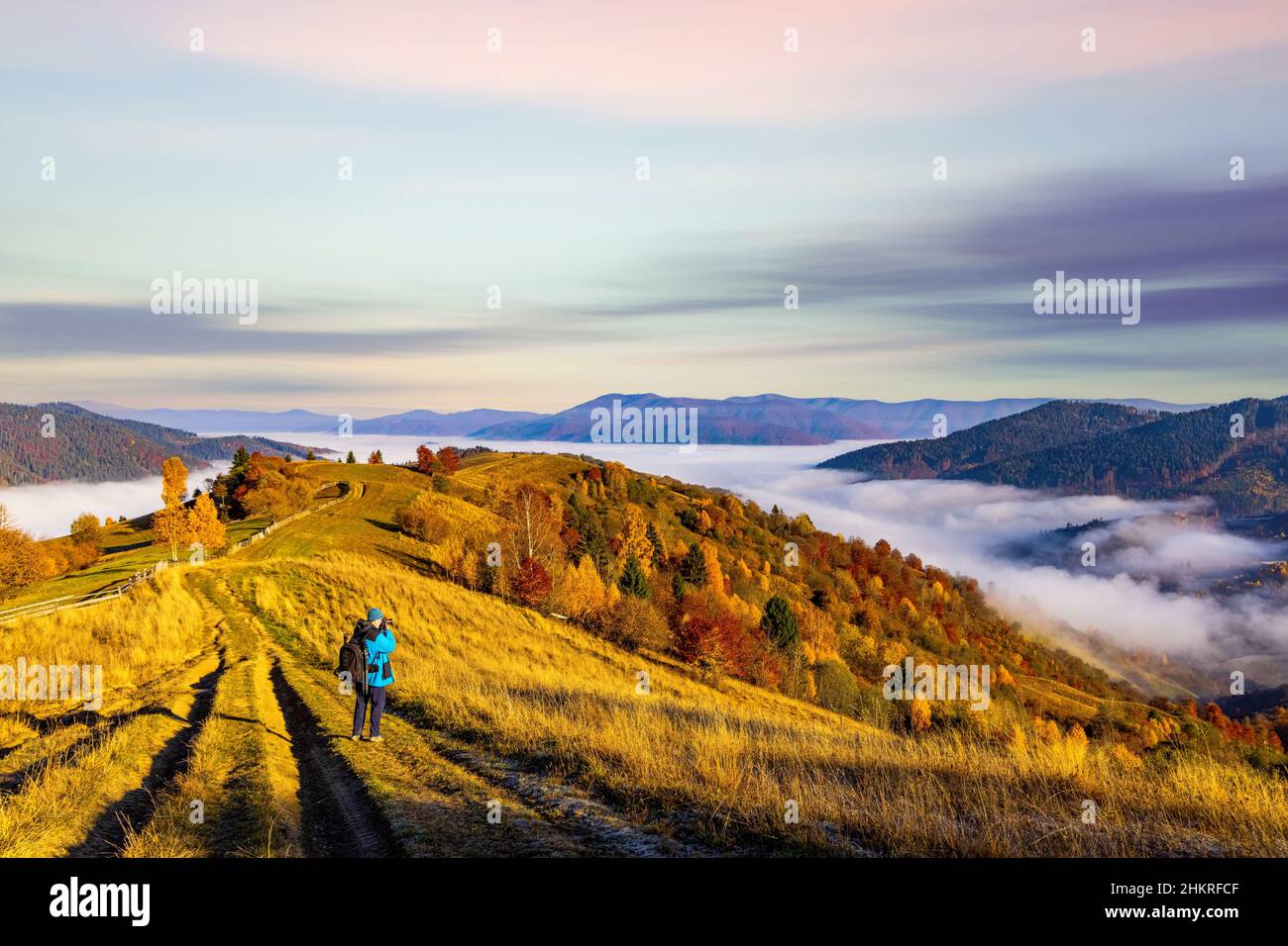 Photographer stands on ground grassy road making photo of autumn ...
