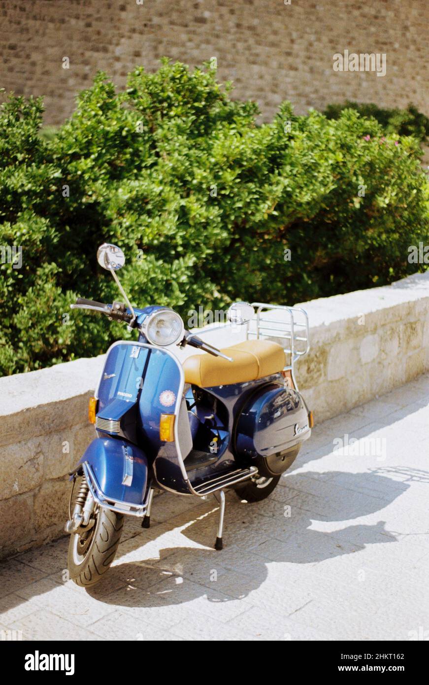 Blue motor scooter stands on paving stones near a stone fence Stock ...