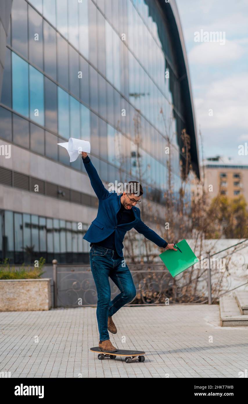 Businessman in his 30s with a suit skating to his work building ...