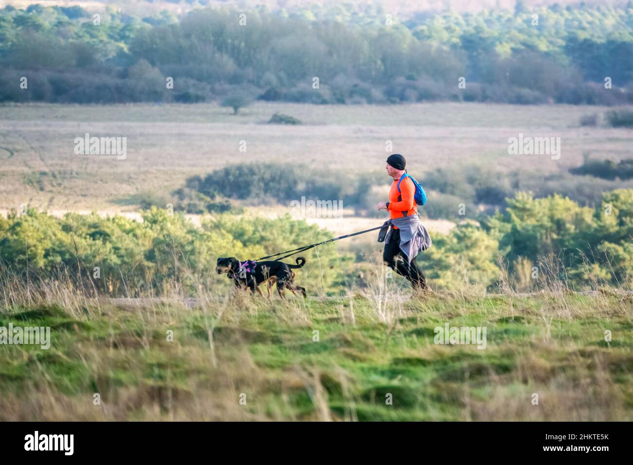 man in a high visibility orange top jogging on an unmade track road ...