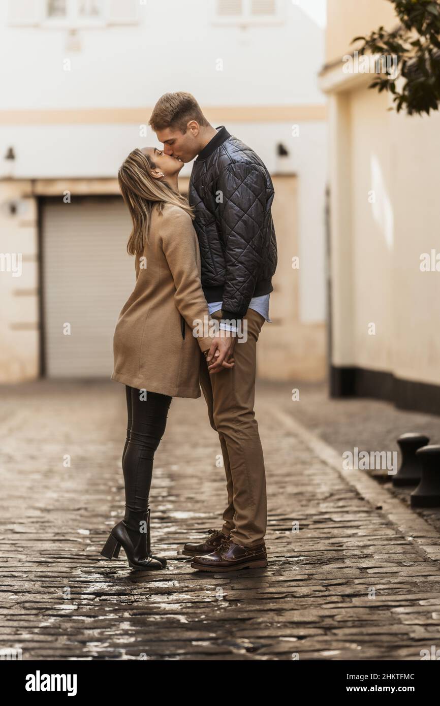 woman stands on tiptoe kissing her partner in the middle of an alleyway ...