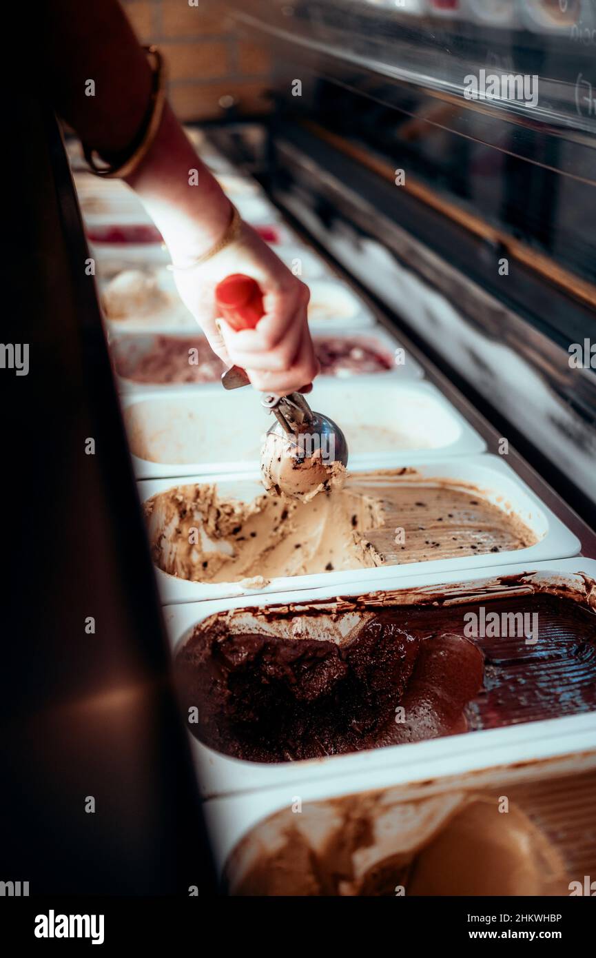 Close-up shot of a female hand scooping ice cream from a metal trays in ...