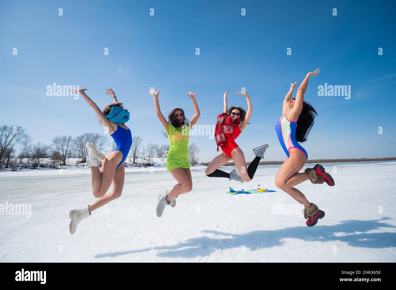Four Caucasian women in swimsuits are fooling around on a snowy beach ...