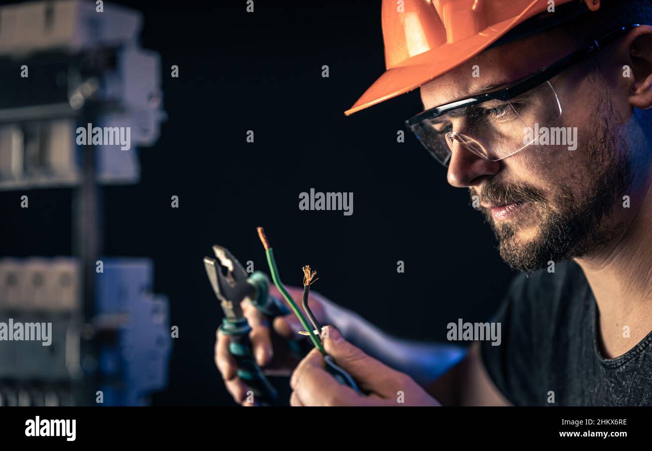 A male electrician works in a switchboard with an electrical connecting ...