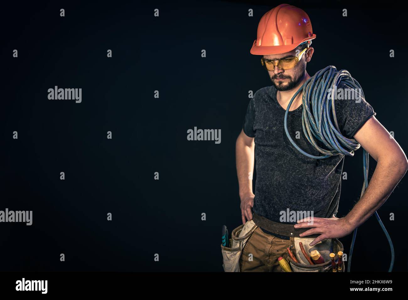 Male electrician with electric cable on a black background, copy space ...