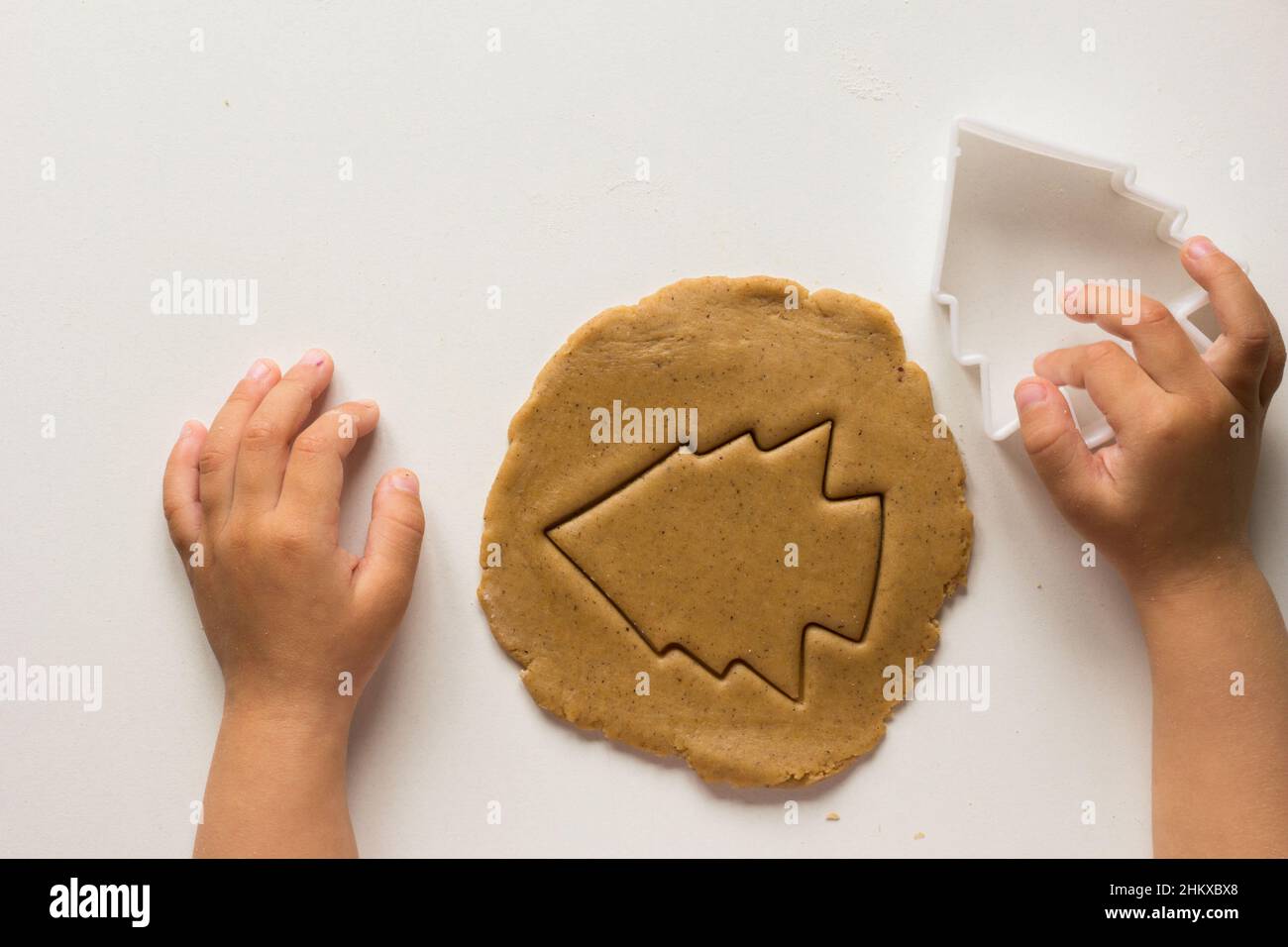 Cutted form of christmas tree on rolled out gingerbread dough by child ...