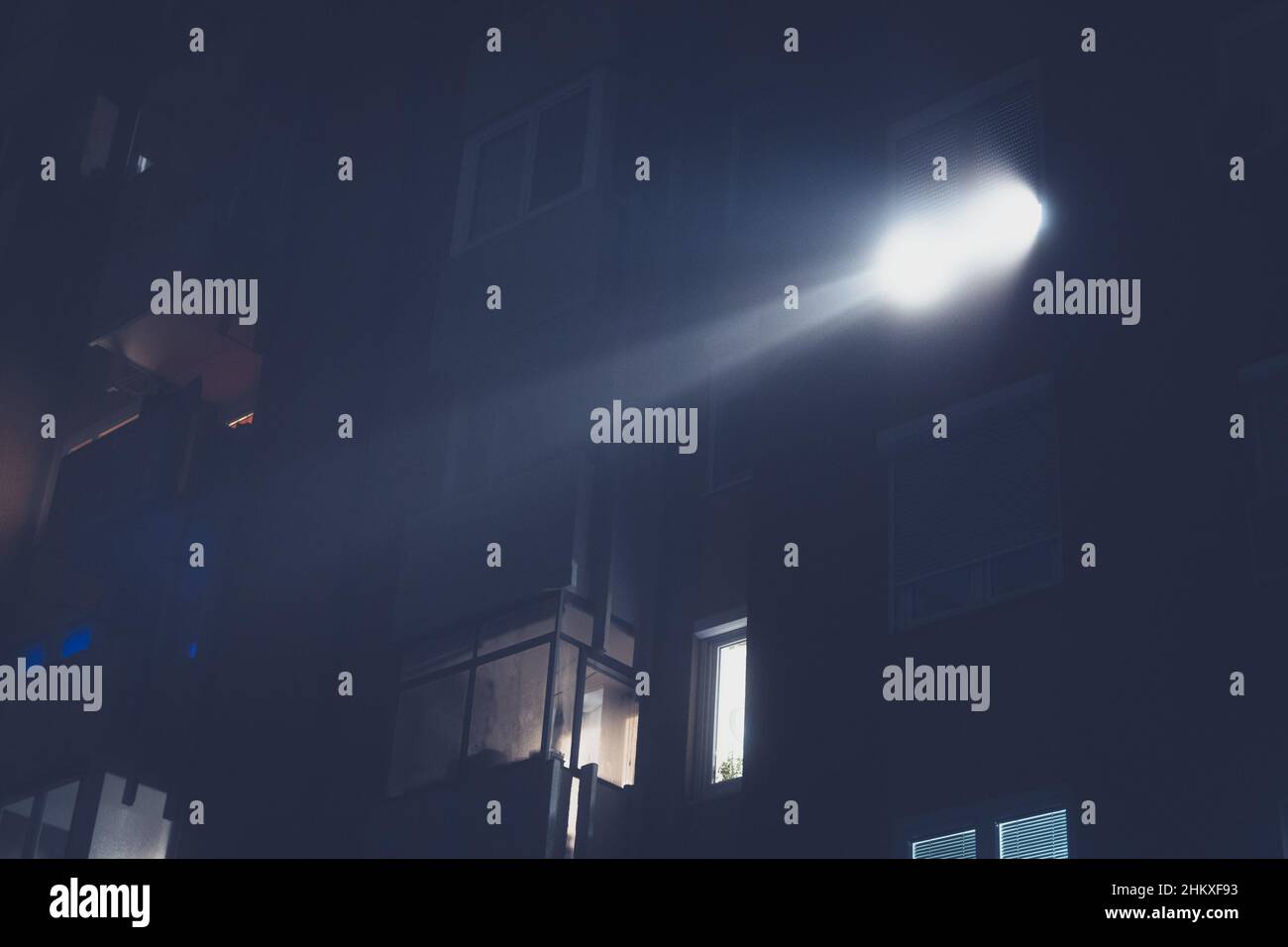 Strong light from an appartment window is pearcing out into thick fog ...