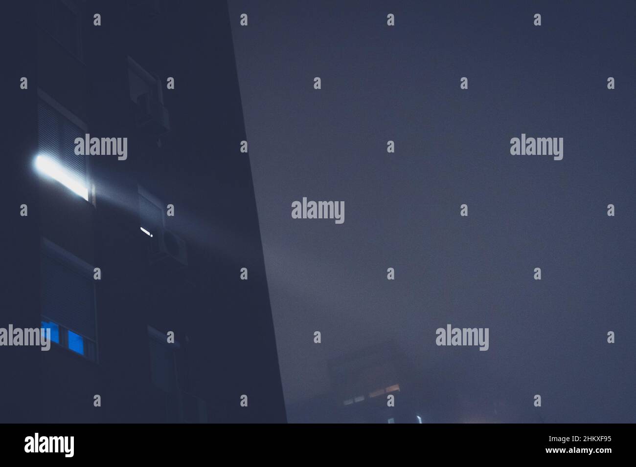 Strong light from an appartment window is pearcing out into thick fog ...