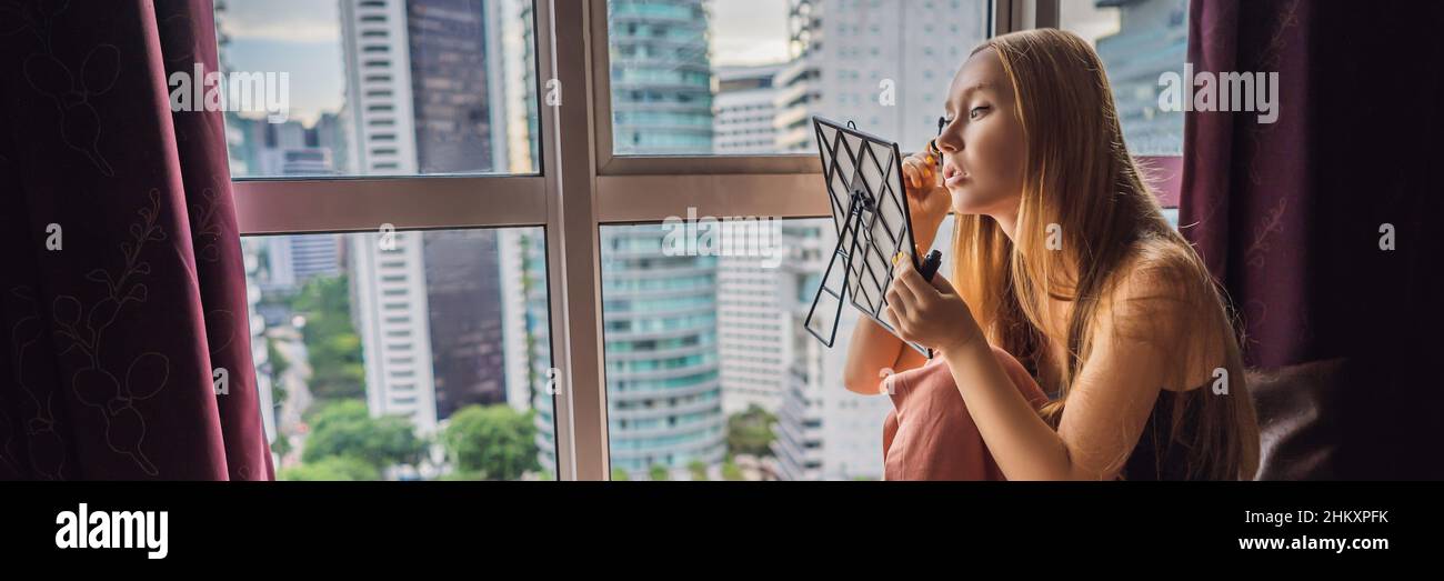 Young woman does makeup sitting by the window with a panoramic view of ...