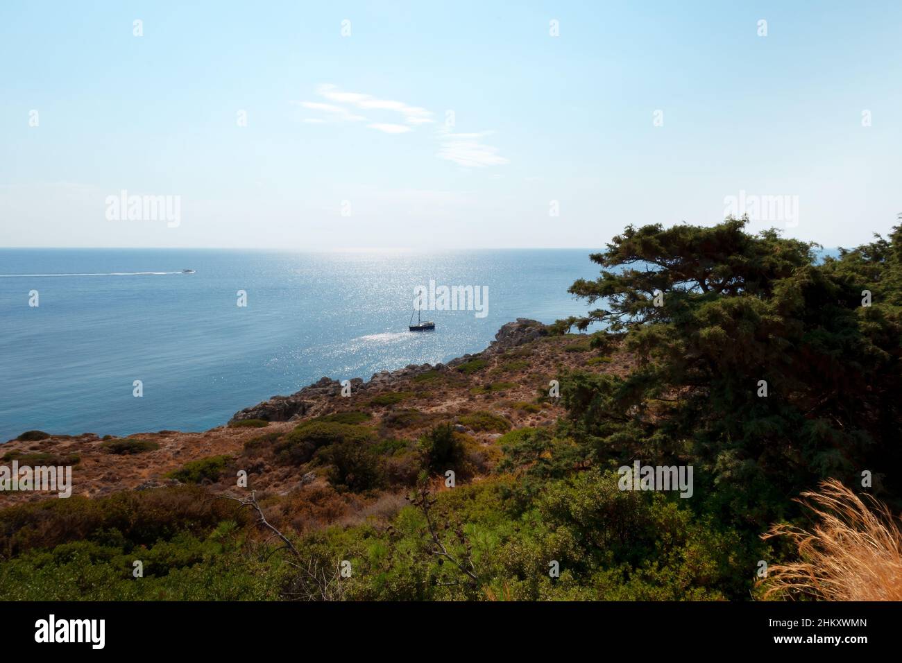 Rocky and shrubby seashore with view of sea blue sky and yacht in ...