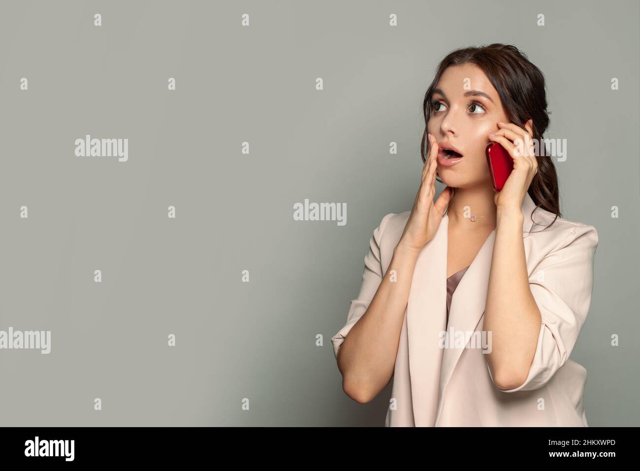 Shocked woman phone on grey studio background Stock Photo - Alamy
