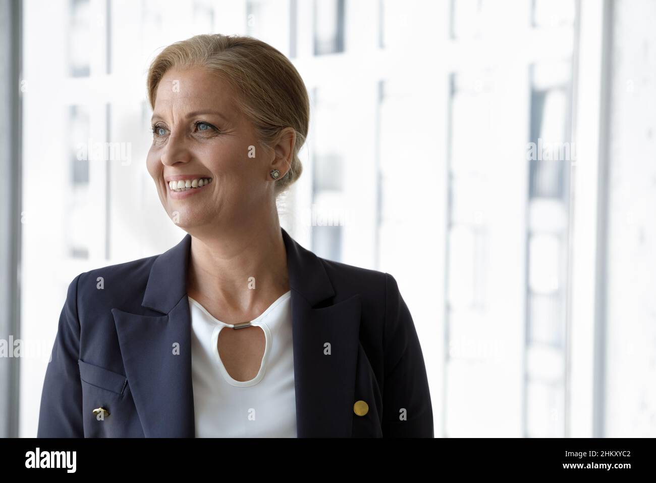 Happy female business leader posing at office window, looking away ...