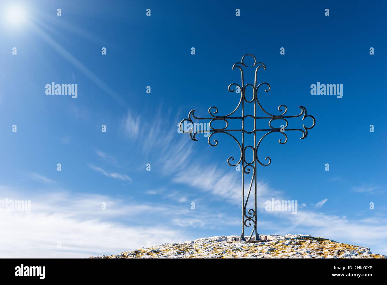 Wrought Iron Religious Cross against a clear blue sky with clouds, sun ...