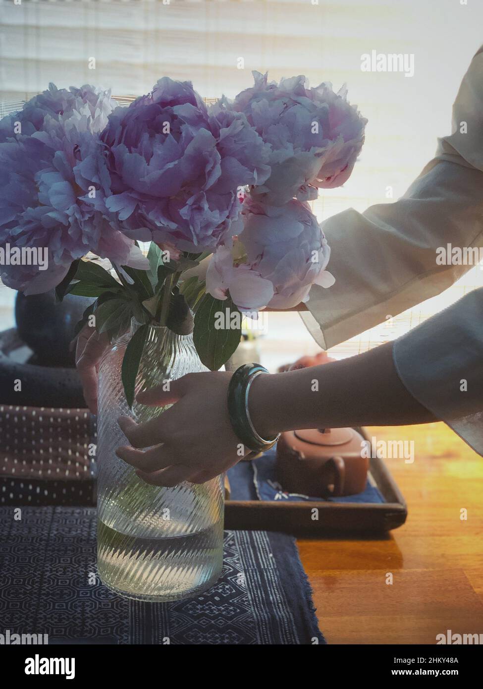 Vertical shot of the hands putting the vase with the bouquet of peonies ...