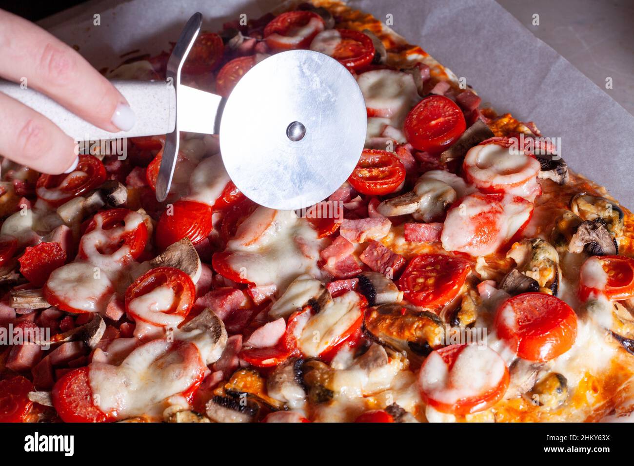 Hand with pizza cutter knife cutting pizza at kitchen table. Close up ...