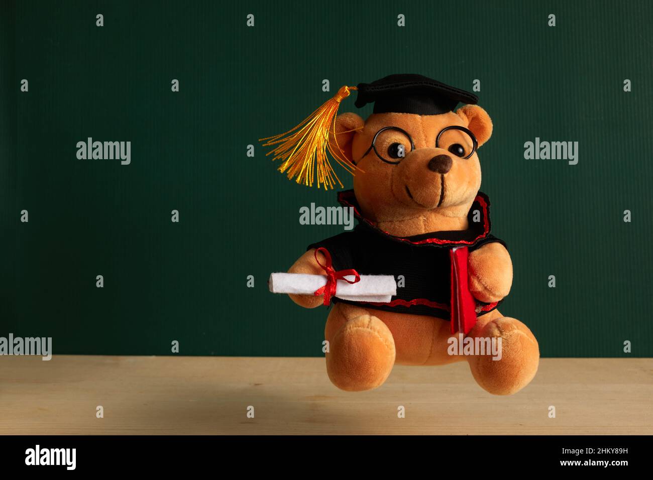 Teddy bear with graduation hat and diploma in front of green chalkboard ...
