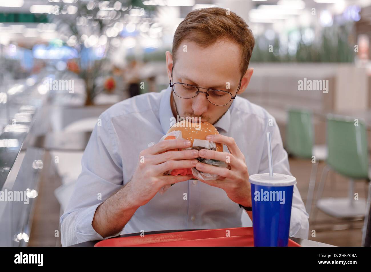 Office worker eating fast food burger and drink soda at food court in ...
