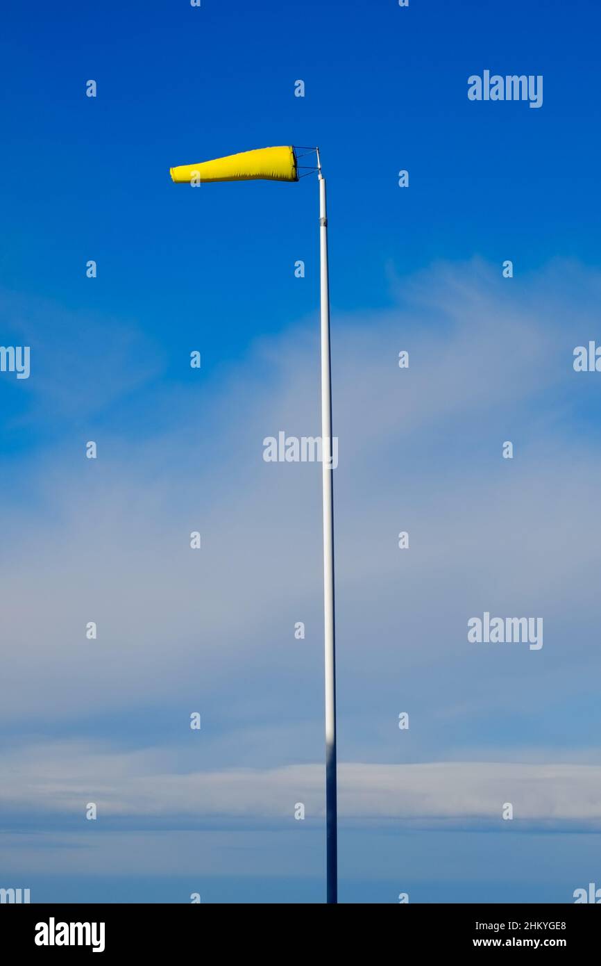 Yellow windsock on a pole against a blue sky with light clouds. Showing ...