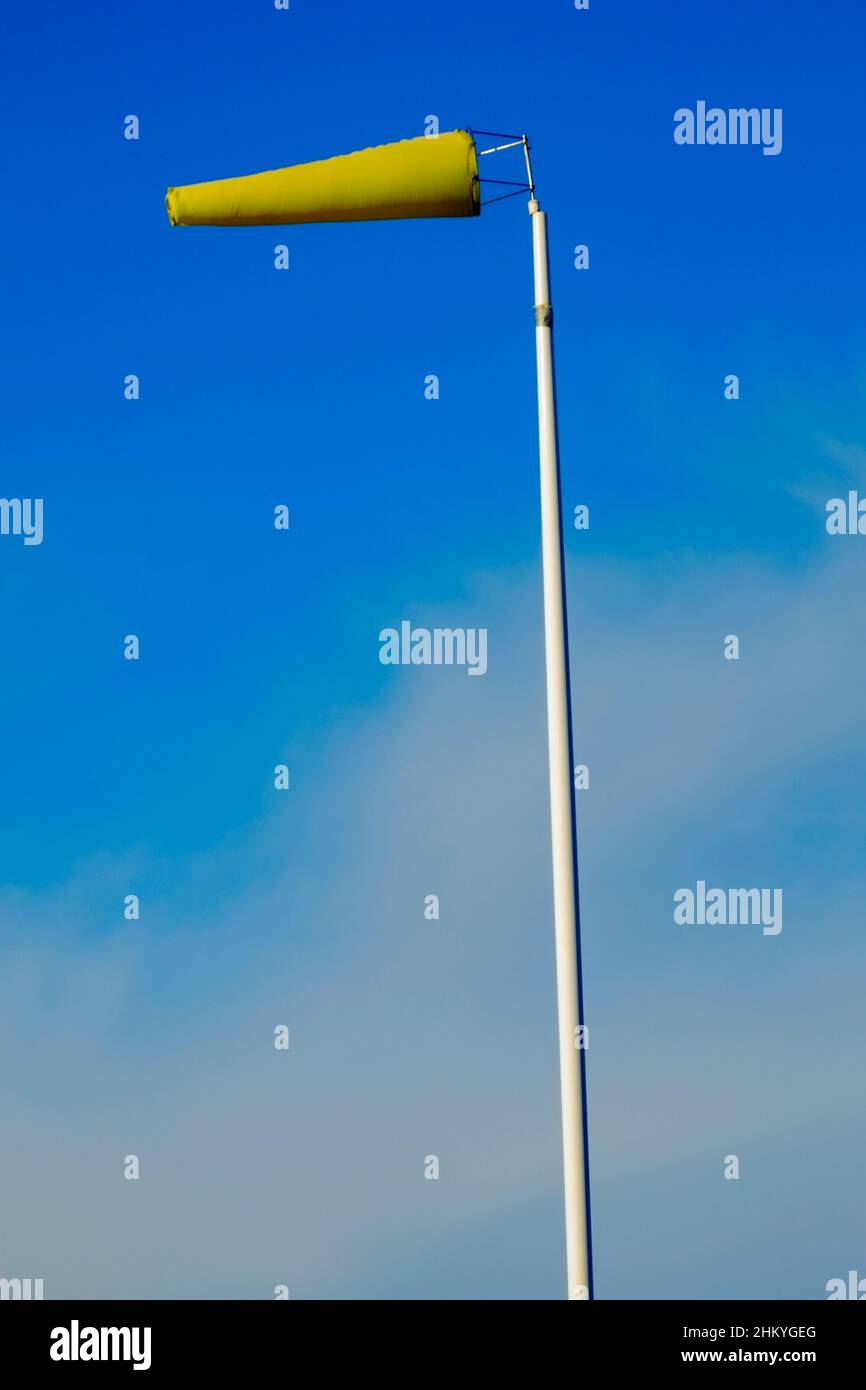 Yellow windsock on a pole against a blue sky with light clouds. Showing ...