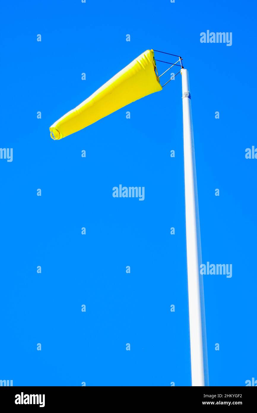 Yellow windsock on a pole against a blue sky with light clouds. Showing ...