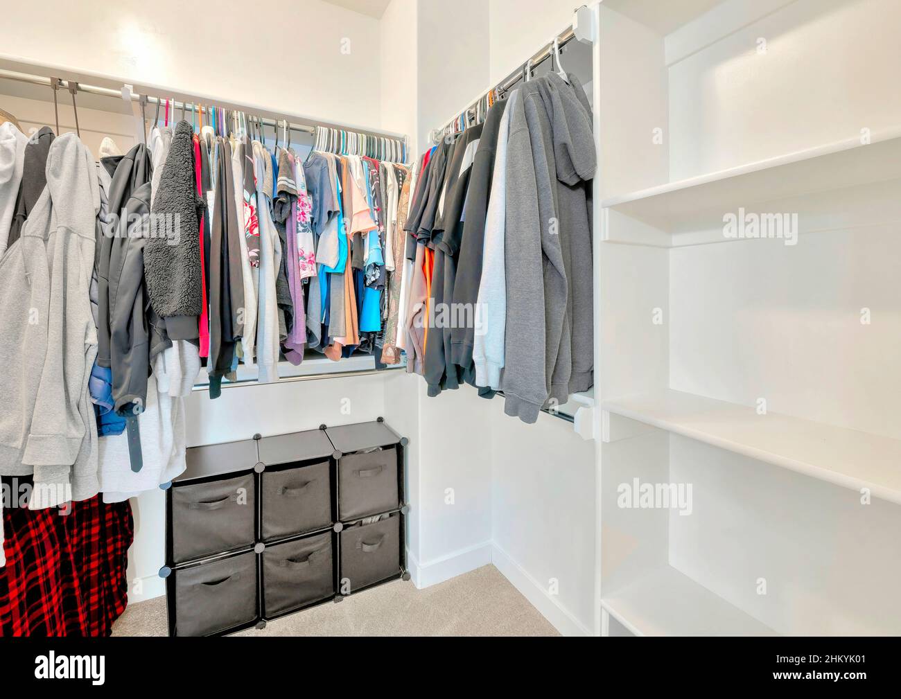 Small walk-in closet with hanging sweaters, shirts and blouse on the ...