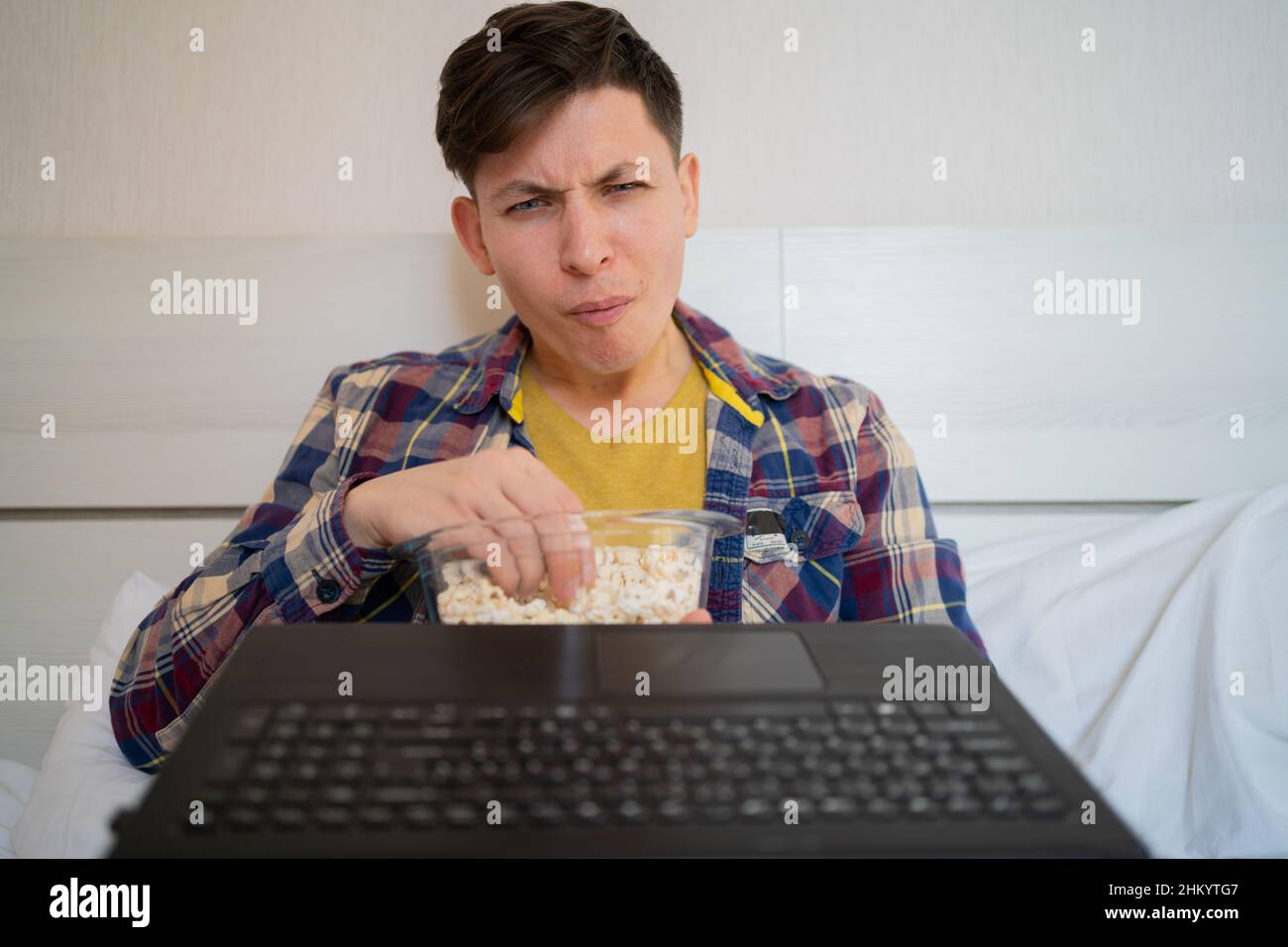 Frustrated man with popcorn hands looks at laptop screen, nervous about ...