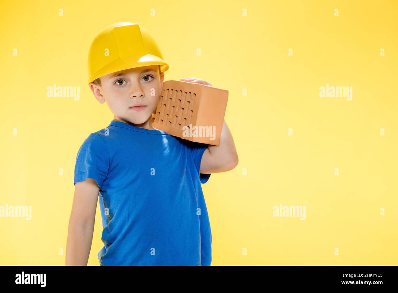 Boy in a construction helmet holds a brick in his hands on yellow ...
