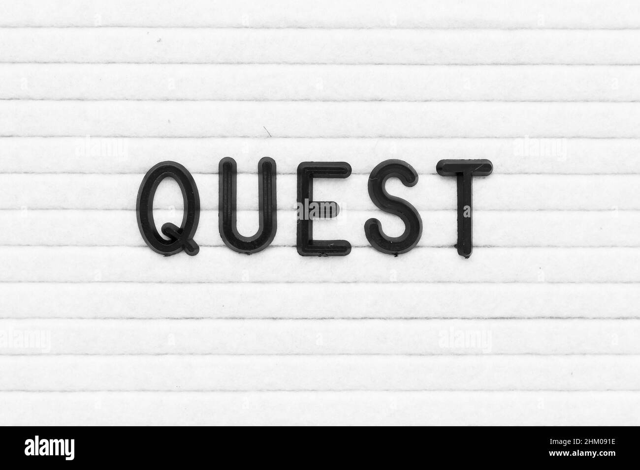 Black color letter in word quest on white felt board background Stock ...
