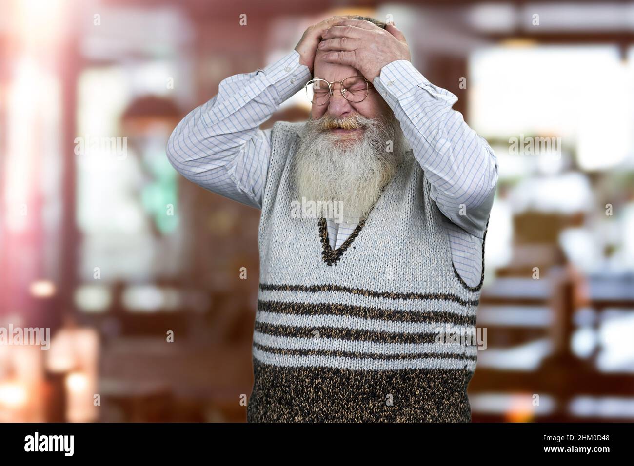 Desperate old man holding his head with frustration. Blur interior ...